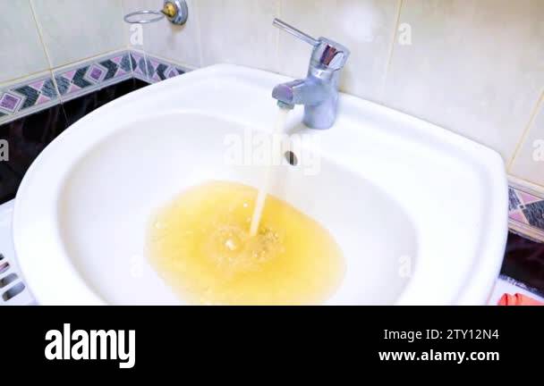 a stream of dirty tap water pours into the sink as an illustration of ...
