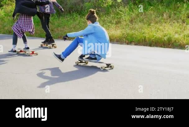 Rear view of cool young caucasian skateboarders skating on downhill at ...