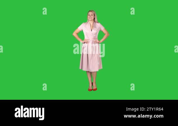 Woman in dress with hands on hips walking while looking at camera on a ...