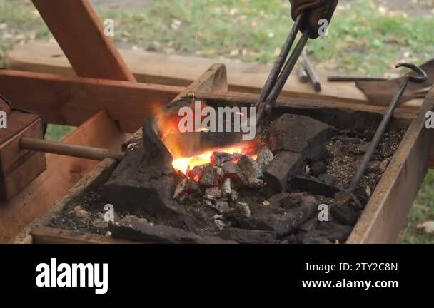 The blacksmith holds the billet over hot coals in a clay oven ...