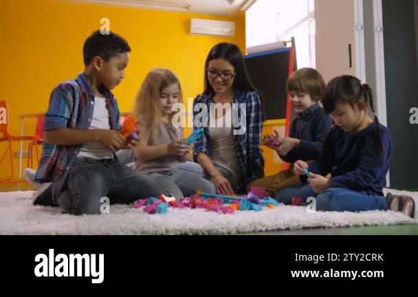 Engrossed multinational diverse kids with cheerful teacher playing with ...