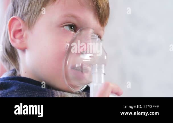 Sick blond boy inhaling through inhaler mask, close-up face side view ...