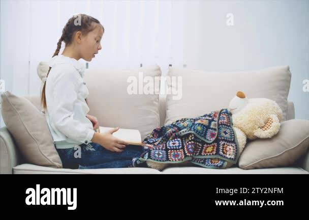 Cute little girl sitting with her legs curled up, reading fairy-tale ...