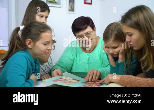 Grandmother and four granddaughters watching old photo album at home ...