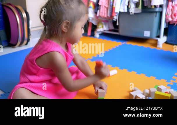 Little Asian cute girl playing cubes, sitting on a color floor. The ...