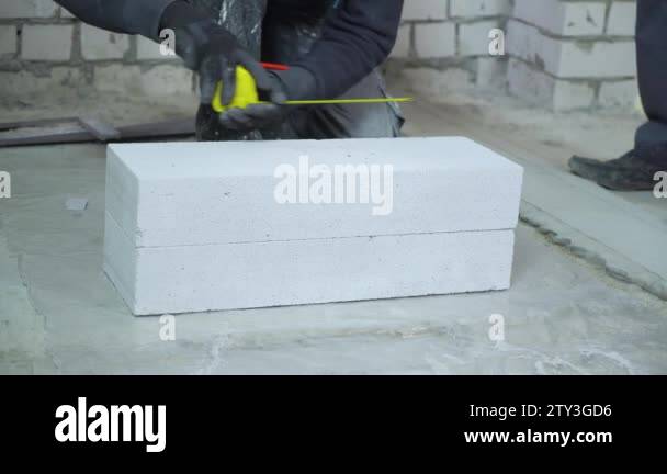 construction worker sawing aerated concrete block after measuring it ...