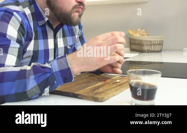 Fat man with a beard in a plaid shirt eats fast food cheeseburger and ...