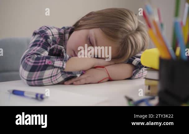 Close-up portrait of tired Caucasian schoolgirl sleeping on the table. Exhausted child getting ...