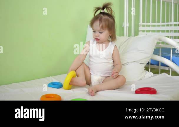 child puts a toy ring on his foot. Baby playing in hospital on bed with ...