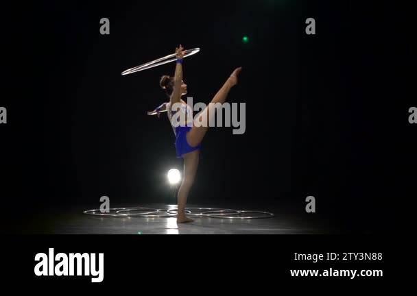 Girl gymnast turns the metal hoop on the arm then on the leg. Black ...