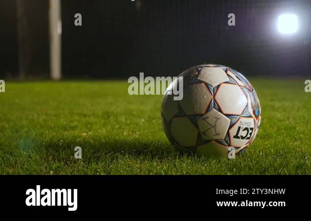Football lying on a playground is hit with a leg in a spiked sneaker in ...