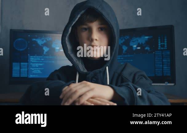 Boy wonder Hacker in hood at data center filled with display screens ...