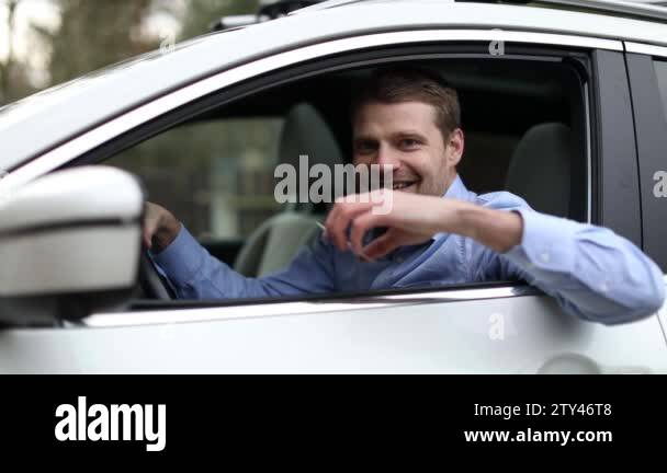 young man sitting in the car and showing his new driver license with ...