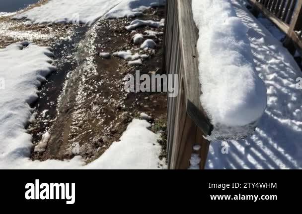 Ice and snow melting on the ground and on the railing of a small wooden ...