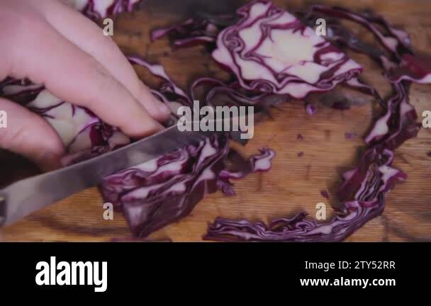 A slices of red cabbage is cut with a steel knife on a wood kitchen ...