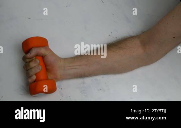 Weak, without muscles male arm does an exercise with a orange dumbbell ...