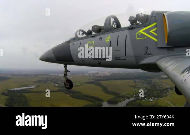 A gray blue combat fighter aircraft flies over the river and fields ...