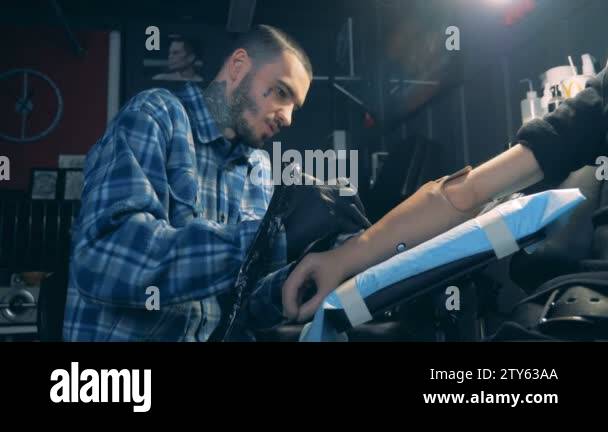 Man uses a machine to draw a tattoo on a prosthetic hand in a salon ...