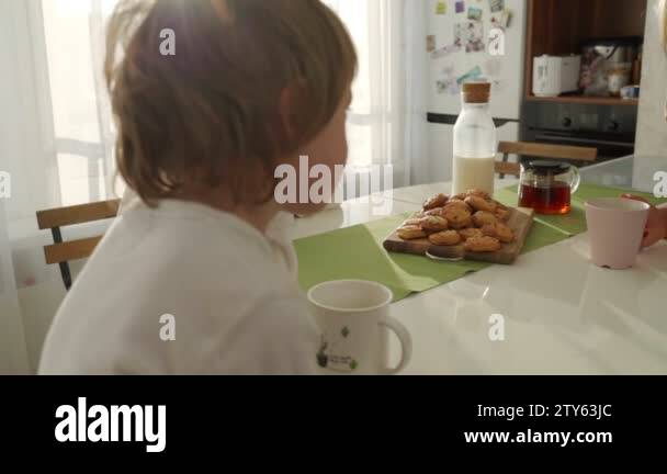 Two boys having breakfast in modern kitchen. Boy eat cookie with milk ...