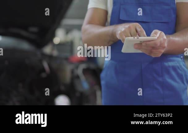 Hands of adult mechanic typing on his cell phone, the car is in the ...