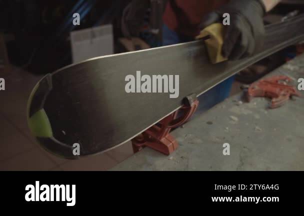 Male worker of ski service workshop doing sharpening and repair of skis ...
