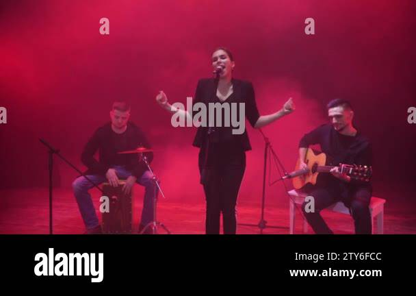 Music band performing on stage in red light and smoke in background ...