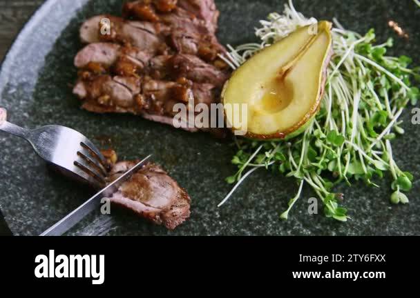 closeup human hands cut off one slice of grilled beef meat by fork and ...