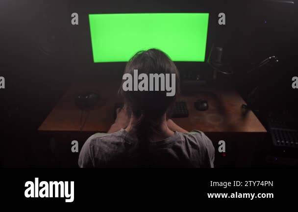 A man with long hair prints text on his keyboard, he has a green screen ...