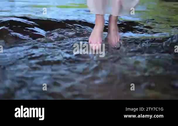 Beautiful barefoot girl dipping her feet into fresh flowing river ...