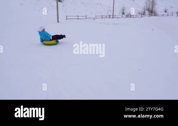 beautiful young woman slides down slide in snow on an inflatable snow ...