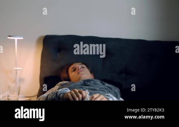 Young sick woman with fever sneezing at night in bed. Medicines ...