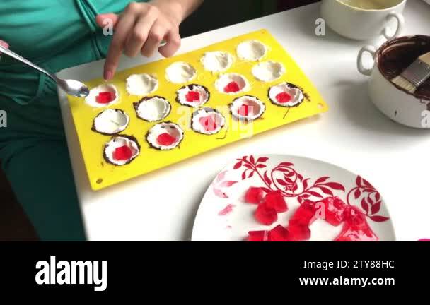 A woman puts strawberry jelly on a curd in silicone mold. The mold is ...