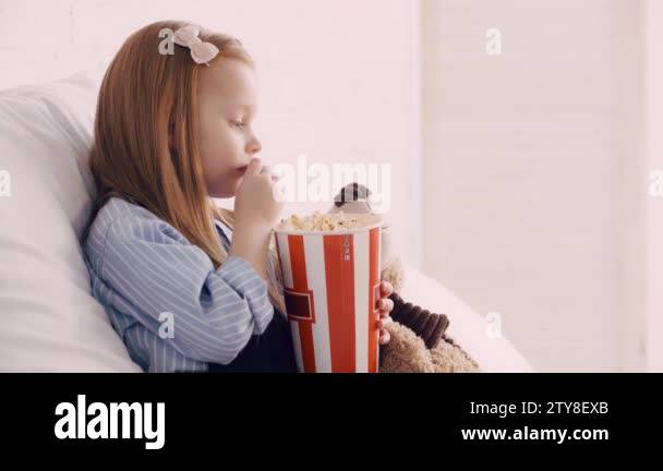 Kid eating popcorn by teddy bear and watching cartoons at laptop in ...