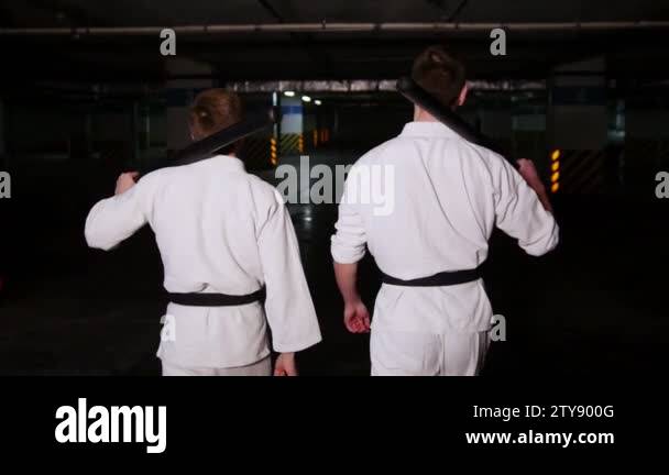 Two men in kimono walking on a parking lot holding a training swords on ...