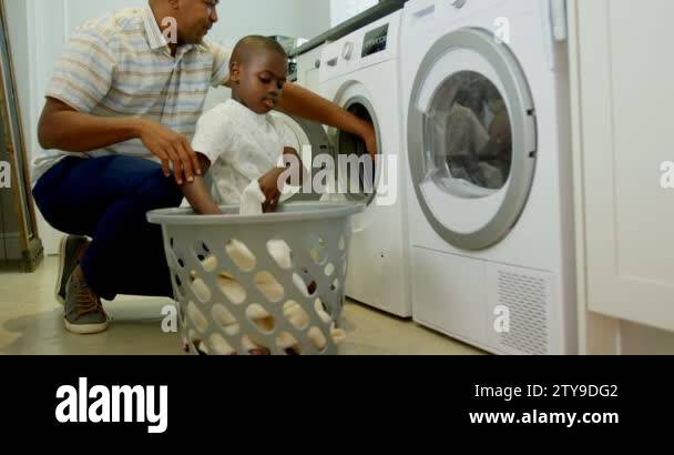 Side view of black father and son washing clothes in washing machine at ...