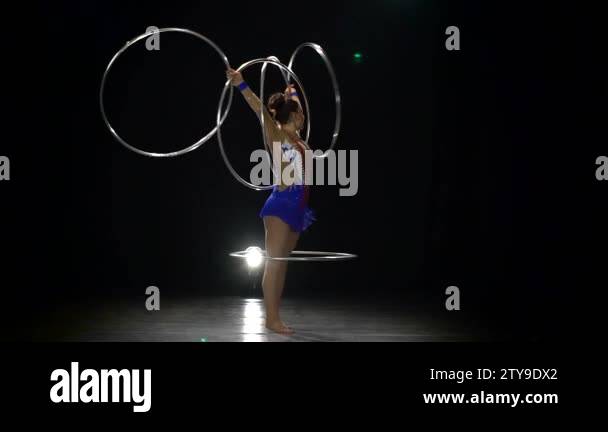 Girl gymnast twists a lot of metal hoops on her body. Black background ...