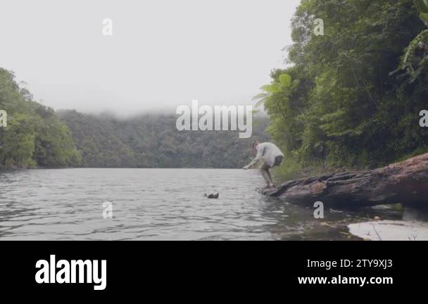 Tourist man washing hands in tropical river flowing among green hills ...
