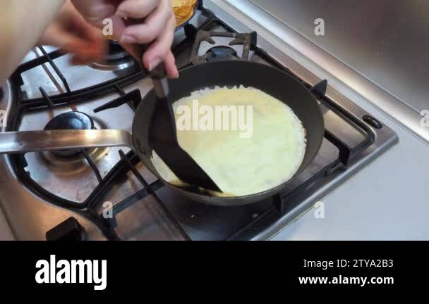 A hand hand turns a pancake with a plastic spatula from one side to the ...