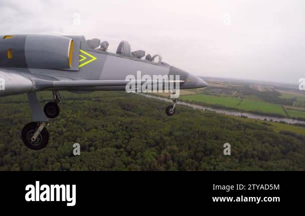 A gray blue combat fighter aircraft flies over the river and fields ...