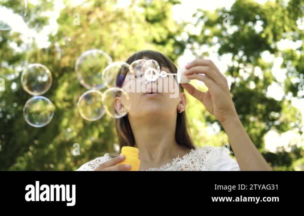 young girl playing in the park and blowing bubbles into the camera lens ...