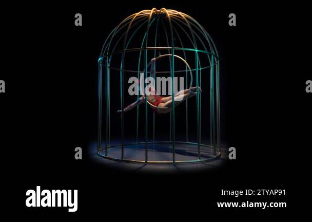 Girl art acrobatics on a rotating hoop in a metal cage . Black ...
