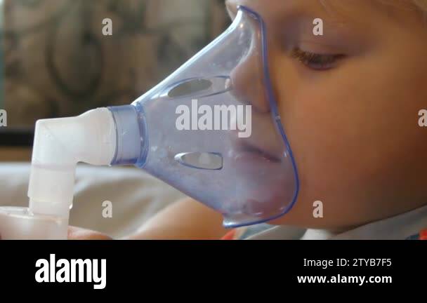 The boy breathes through an oxygen mask. The child takes inhalations ...