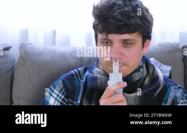 Sick man inhaling through inhaler nozzle for nose sitting on the sofa ...