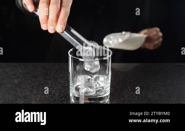 Close-up shot of female bartender putting ice cube into alcoholic beverage in slow motion ...