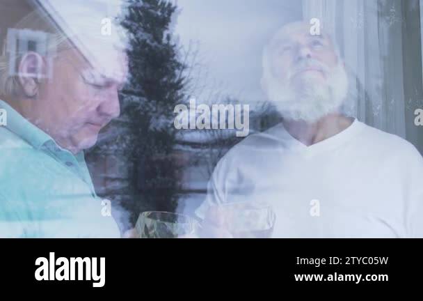 Two old men drinking alcohol whiskey standing near the window at home ...