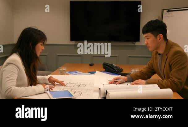 Side view of young Asian business people discussing over blueprint in ...