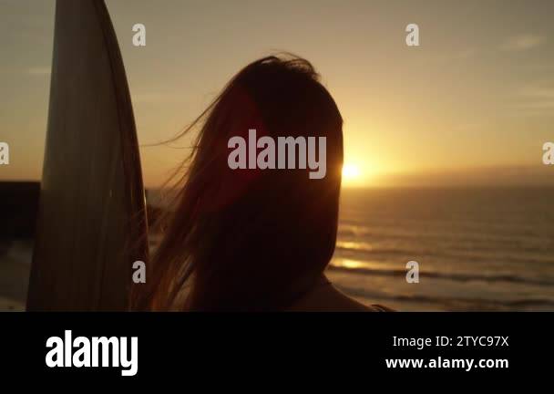 SLOW MOTION CLOSE UP: Unrecognizable girl with long flowing hair gazing at golden sunset giving ...