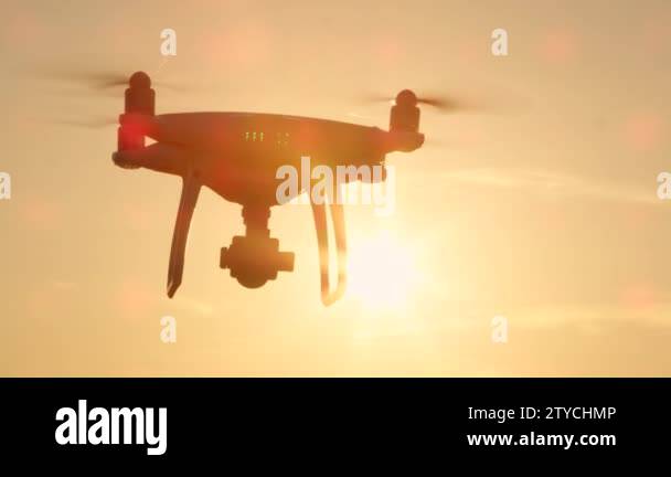 CLOSE UP LENS FLARE SILHOUETTE Small filming drone flying over golden ...