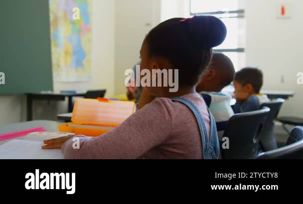 Side view of diverse group of students applauding in classroom at school. Male teacher looking ...