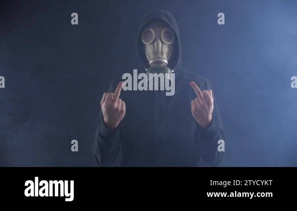 Man in a gas mask shows the middle finger in a smoke-filled dark room ...